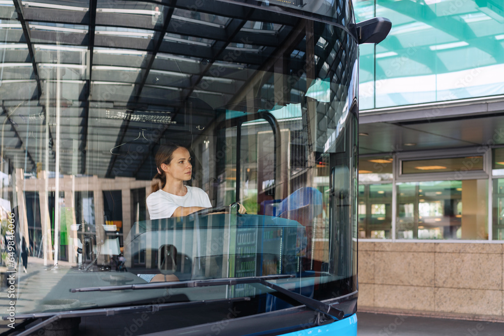 Young woman driving a shuttle bus at a suburban bus station, female ...