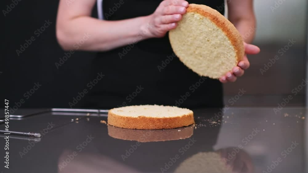 Professional confectioner in black apron connecting cut cake layers ...