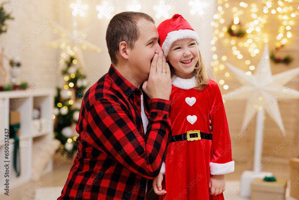 Father whispering secret to his daughter in red santa costume in ...