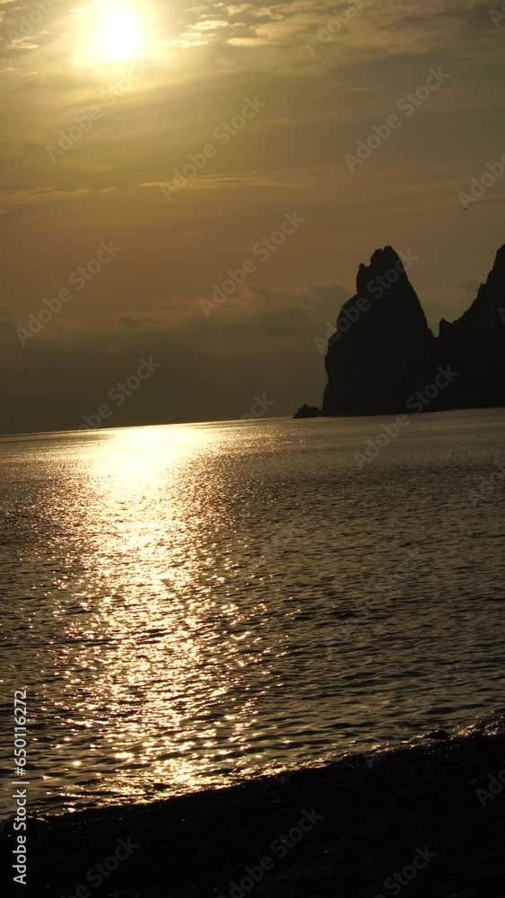 A red burning sunset over sea with rocky volcanic cliff. Abstract ...