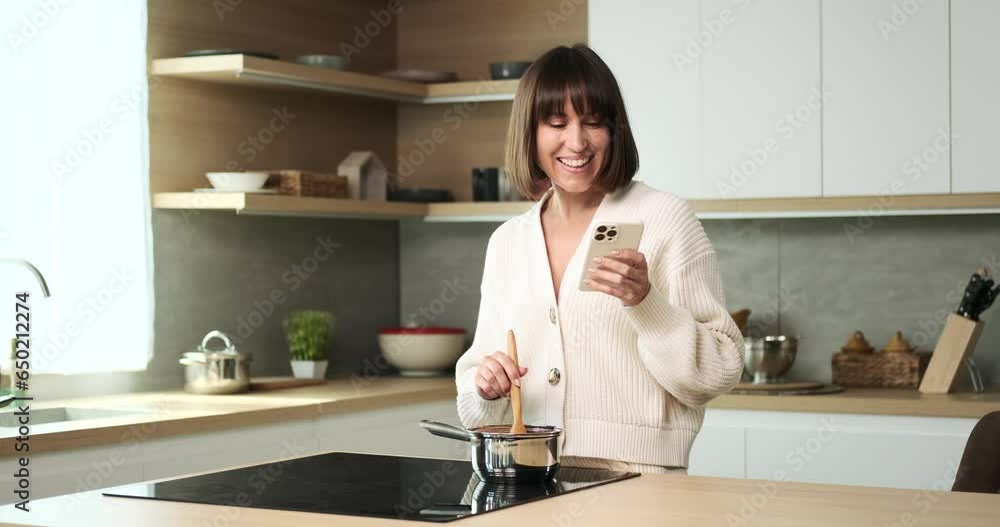 A Caucasian woman multitasks with ease, preparing a meal in the kitchen ...