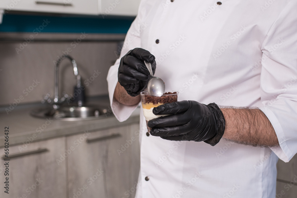 Close-up of a male pastry chef decorating a dessert in the kitchen, a ...
