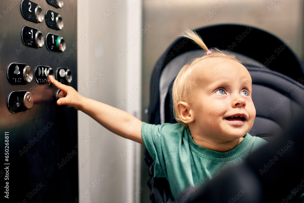 Tiny cute baby sitting in a baby stroller presses the floor button in ...