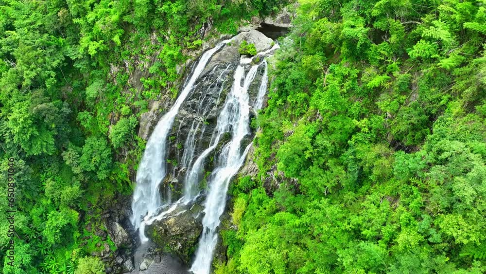 The waterfall is surrounded by a dense, evergreen tropical forest, adds ...