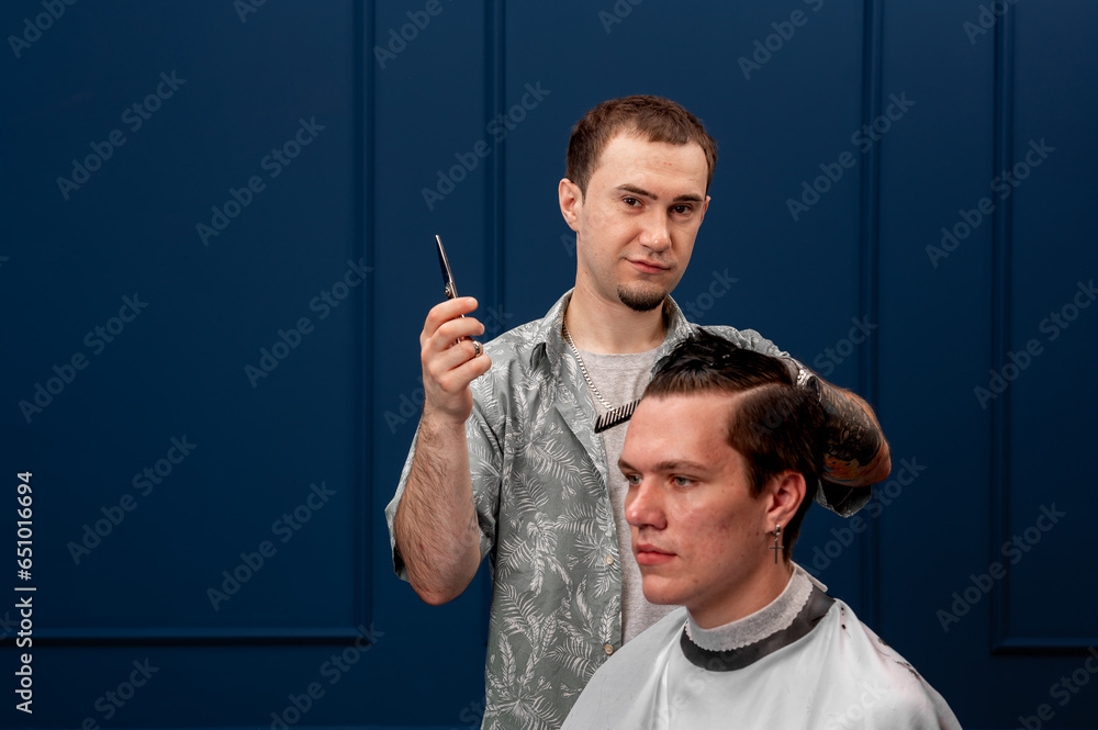Focused Caucasian male hairdresser cuts a Caucasian guy's hair in a ...