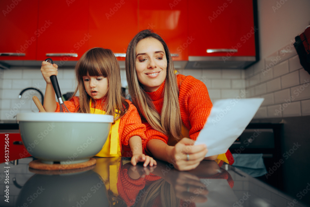 Mother Checking A Recipe While Cooking Next To Her Daughter Mom And