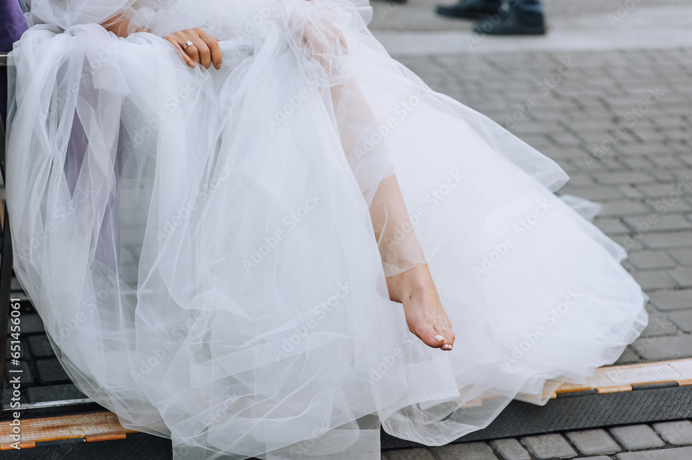 The bride in a long white dress sits, resting without shoes, barefoot ...