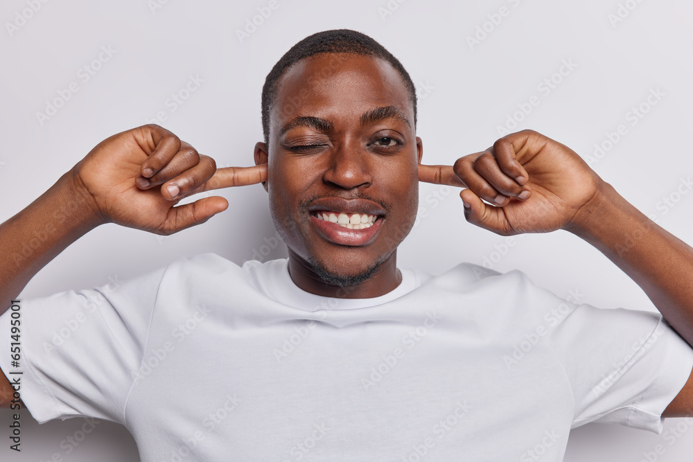 Discontent dark skinned man plugs fingers in ears not listening to loud ...