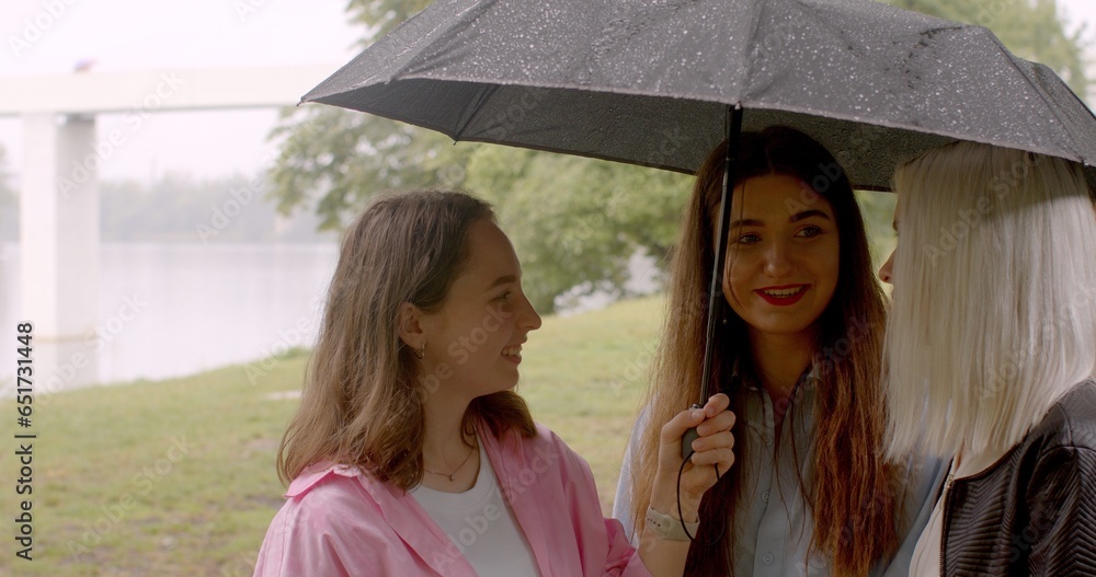 Portrait of three female friends caught in the rain, engaging in ...