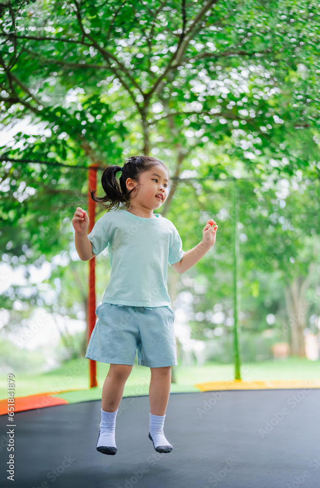 Asian child girl is jumping on trampoline on playground background ...