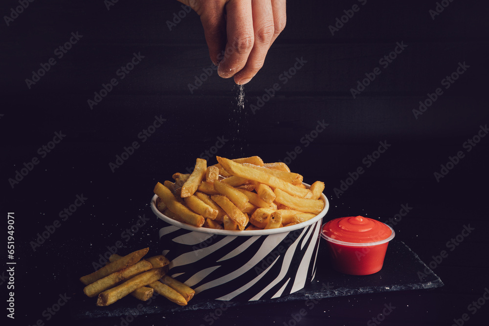 Homemade crispy French fries on a paper bowl with ketchup and a pinch ...