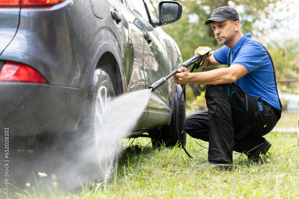 Man professional in protective clothing washing his car in the backyard ...