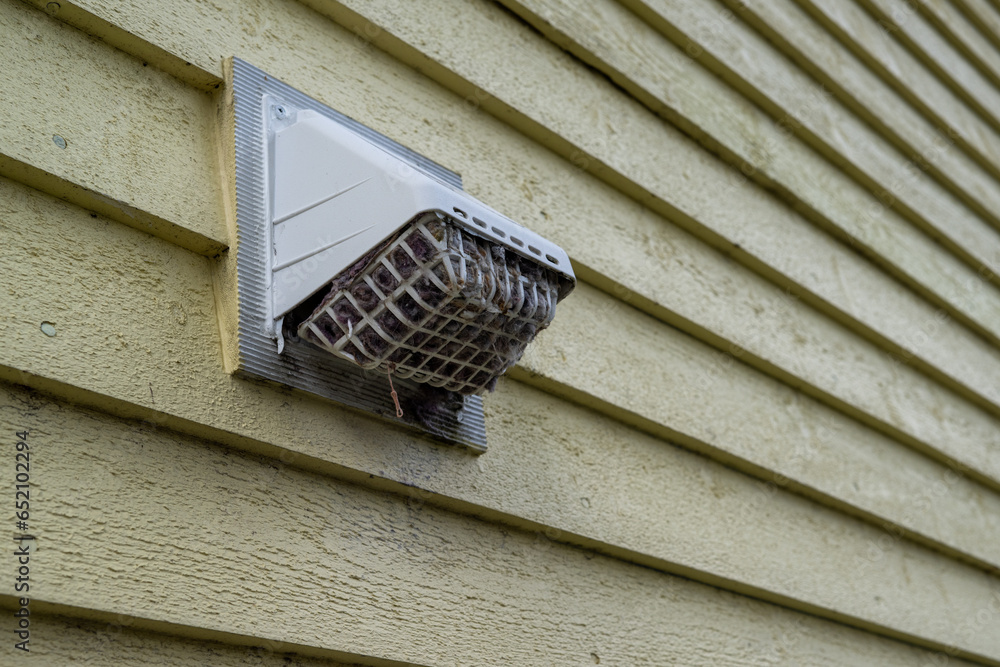 The exterior of a bright yellow house wall with a white dryer vent ...
