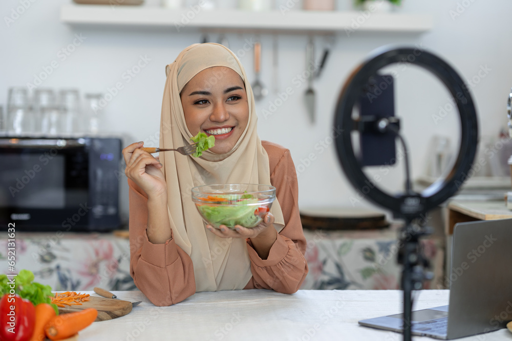 A young Muslim woman in a hijab prepares a vegetable salad and ...