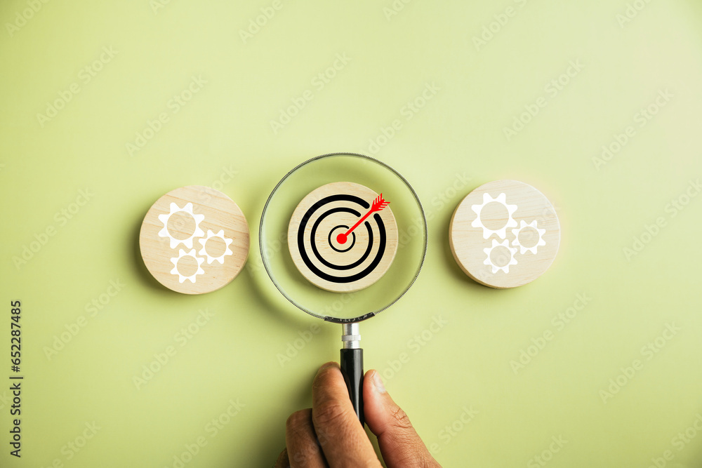 Hand holds a magnifier, focusing on a target icon to analyze objectives ...