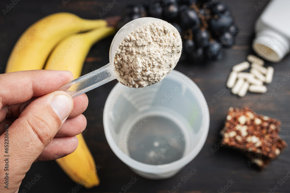 Male hand puts into a shaker scoop portion of whey, soy protein powder ...