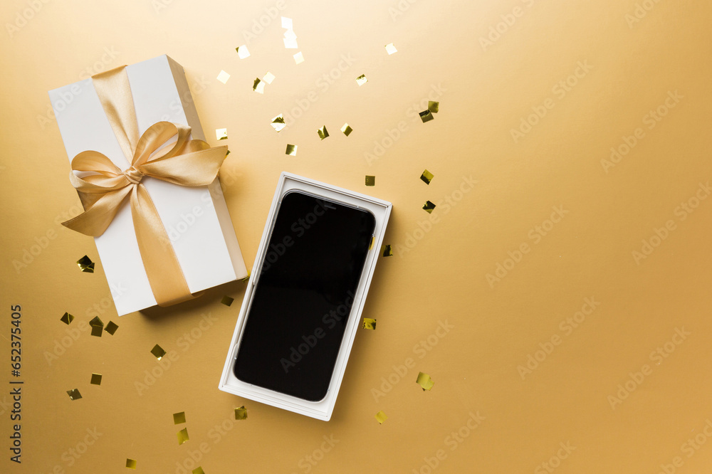 Opened gift box with gold ribbon and smartphone on color background ...