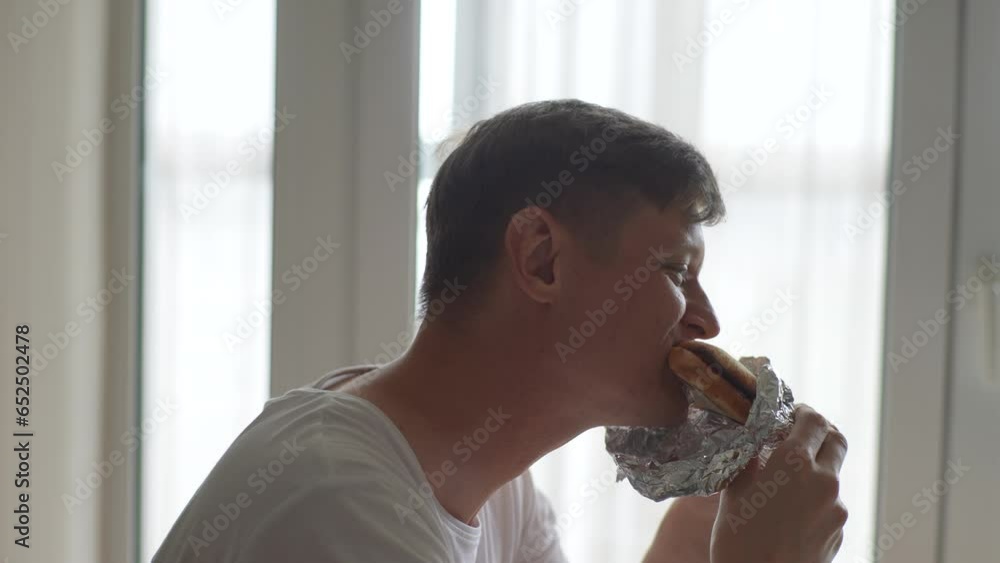 Close-up side view of hungry man eating delicious sandwich at home on ...