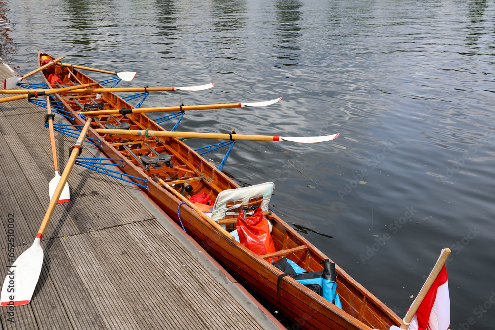 Ein Ruderboot, Mehrsitzer hat an einem Steg an einem Boothaus fest ...