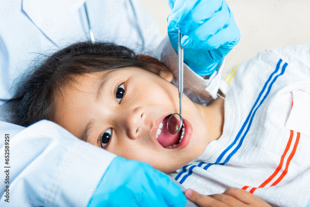 Dental kid health examination. Doctor examines oral cavity of little child uses mouth mirror to ...
