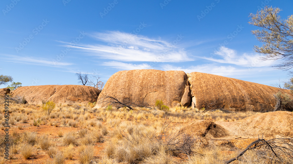 Large smooth granite outcrop between dry grass landscape and blue sky ...