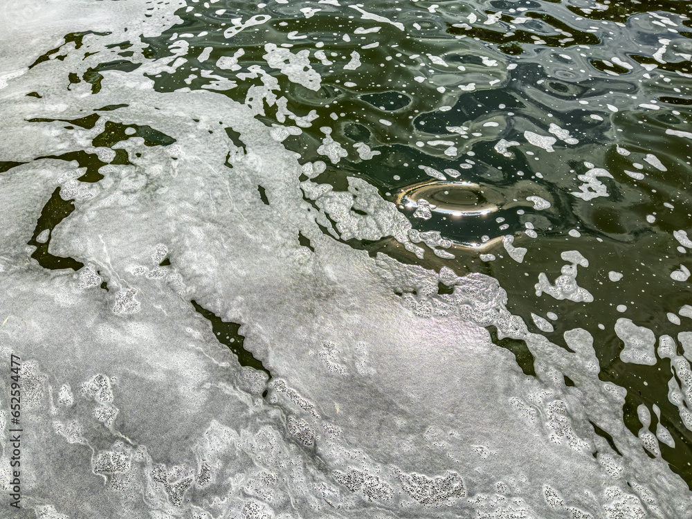 white foam and bubbles on dark polluted water surface. waste water ...
