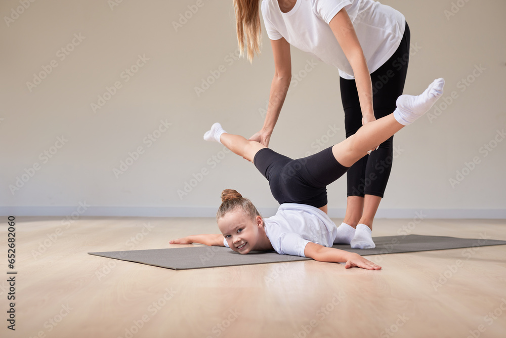 Beautiful female teacher helps a little girl stretch in a gymnastics ...