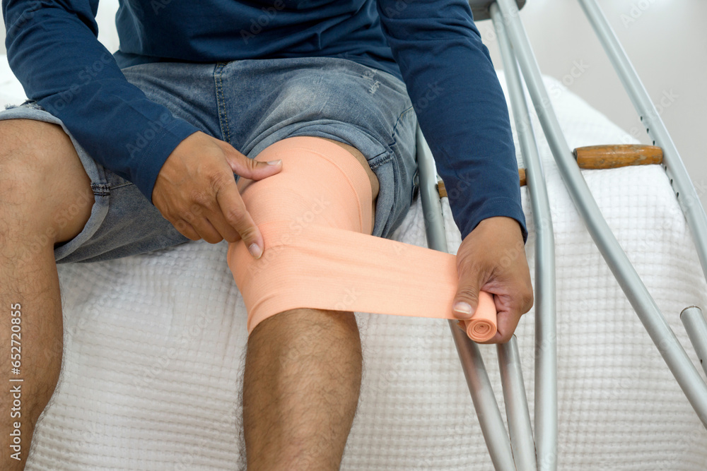 A man with a broken knee sitting on his bed. He leans on crutches ...