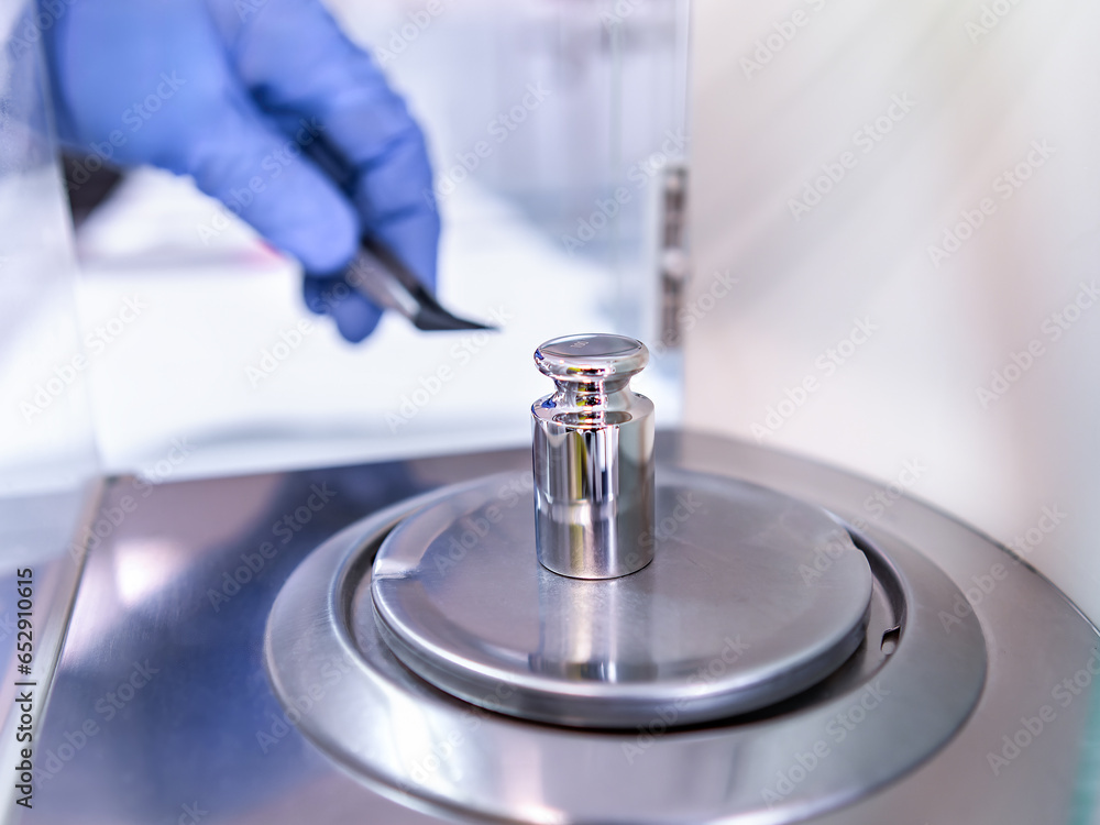 A operator's hand is holding steel calibration weight to place on the ...