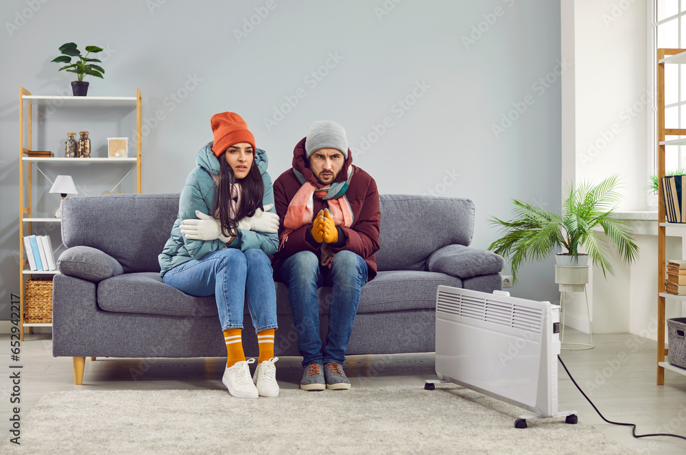 Foto de Freezing people in winter jackets sitting on sofa at home. Sad ...
