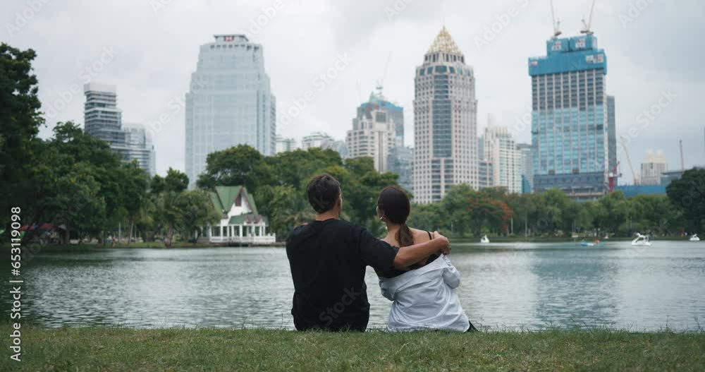 Rear view, romantic couple sits against the backdrop of lake in city ...