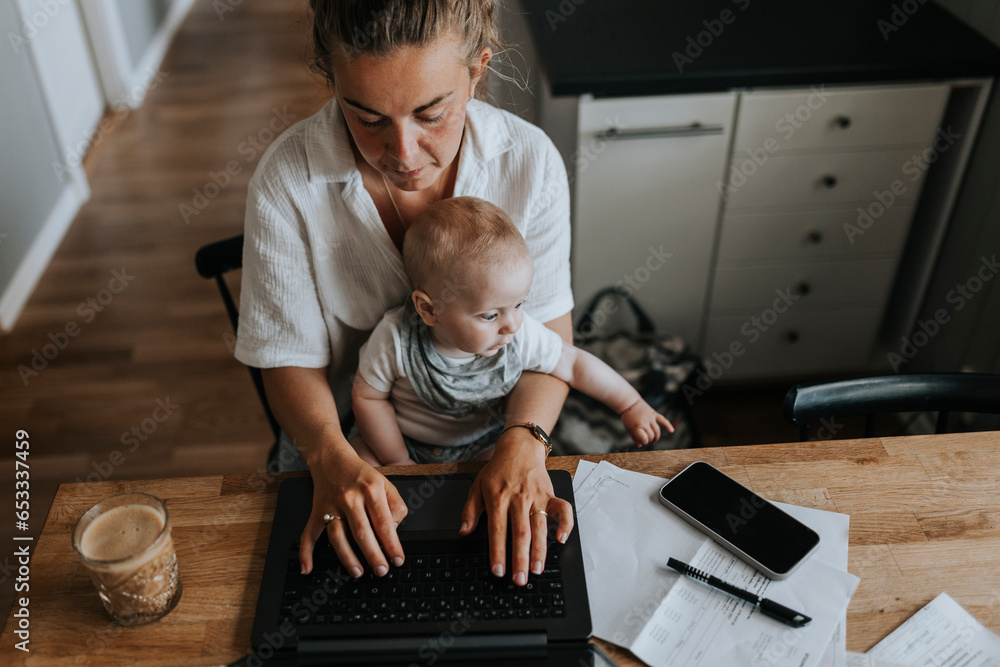 Multitasking mother taking care of baby and working from home Stock ...