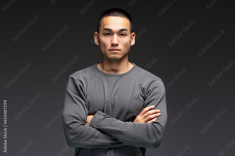 Poster Serious, emotionless young Asian man standing isolated on black ...