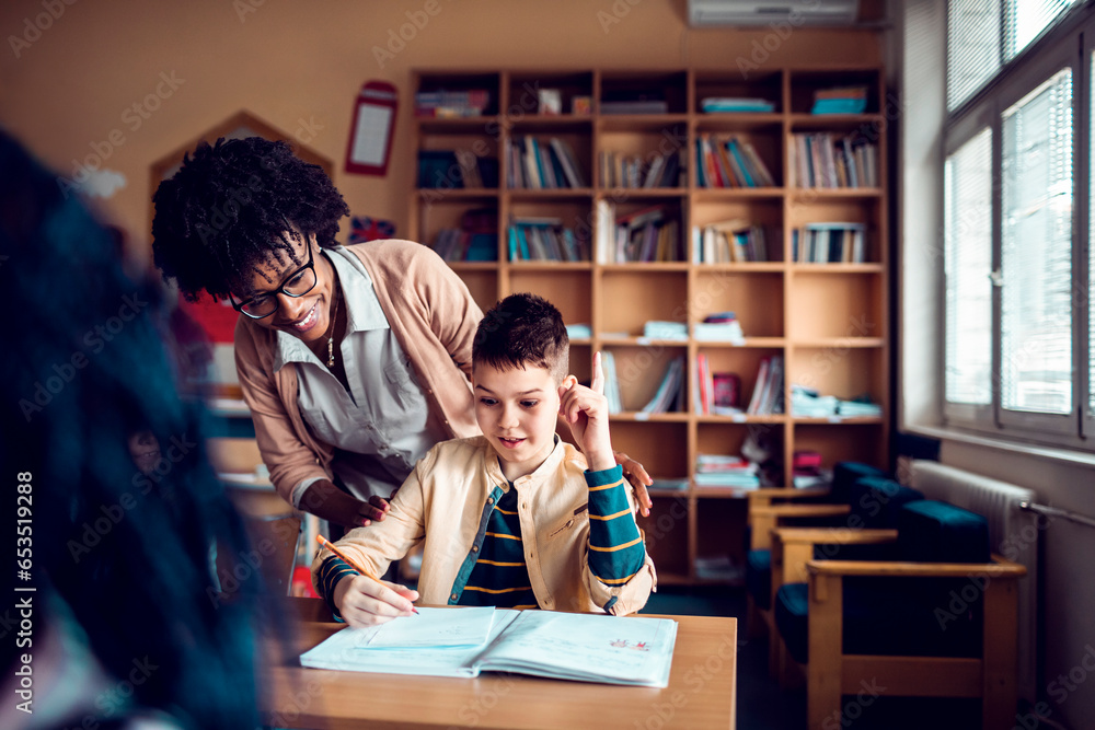 Young Caucasian boy asking for help from his teacher while at the ...