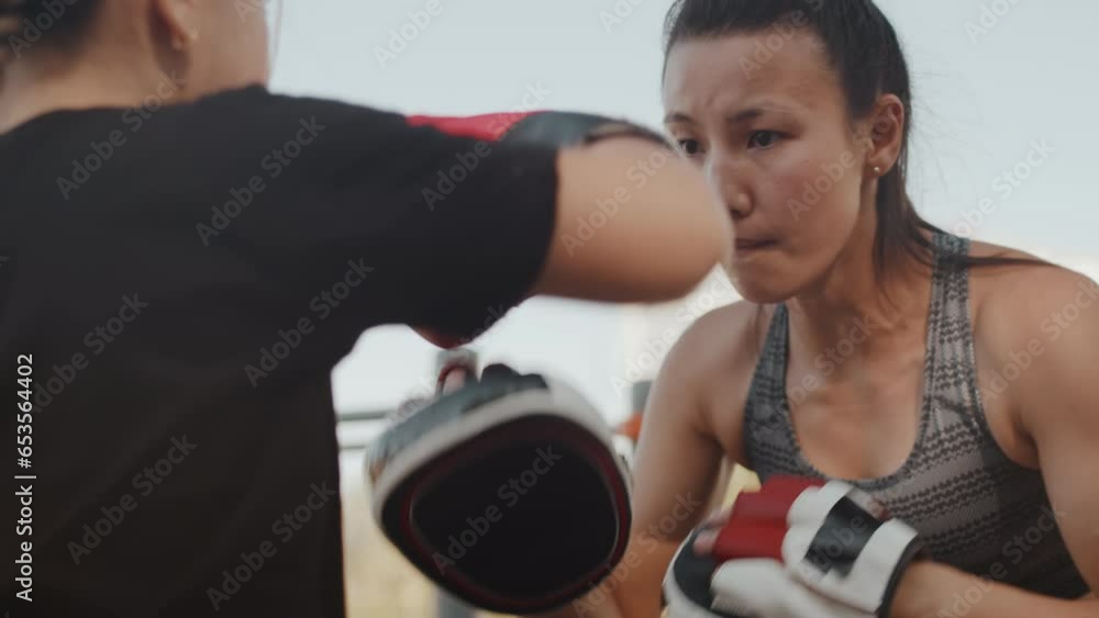 Young asian trainer in boxing paws with a focused face trains a young ...
