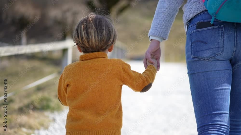 Back of child holding hands with mom walks in outdoor pathway forward ...