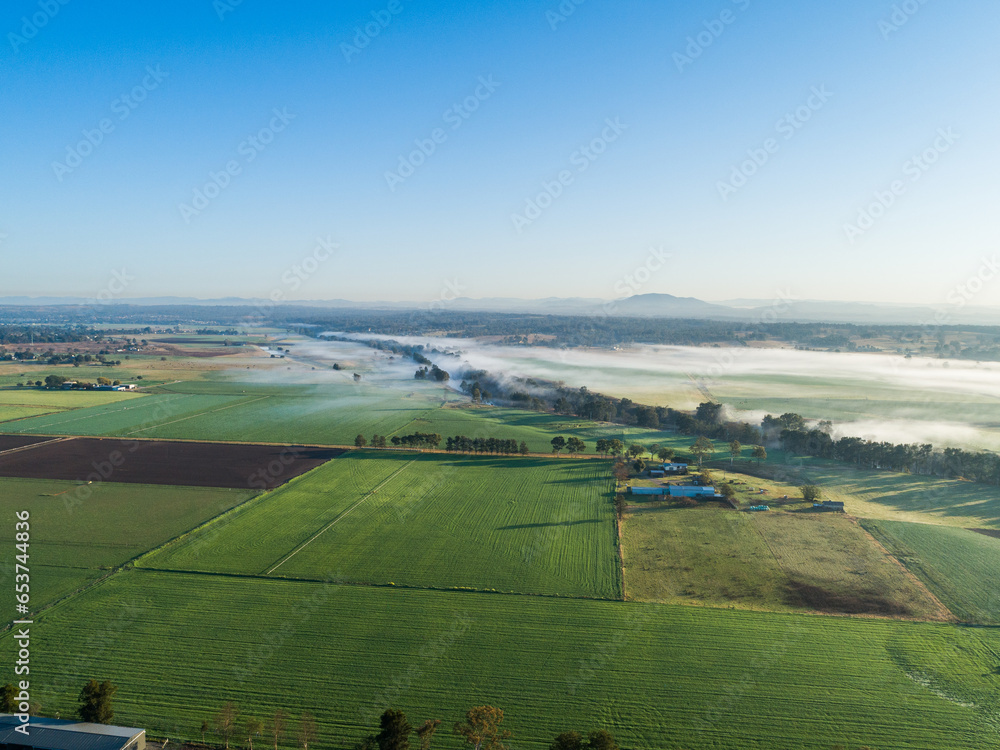 Paddocks of green crops and farm house beside river with mist on ...