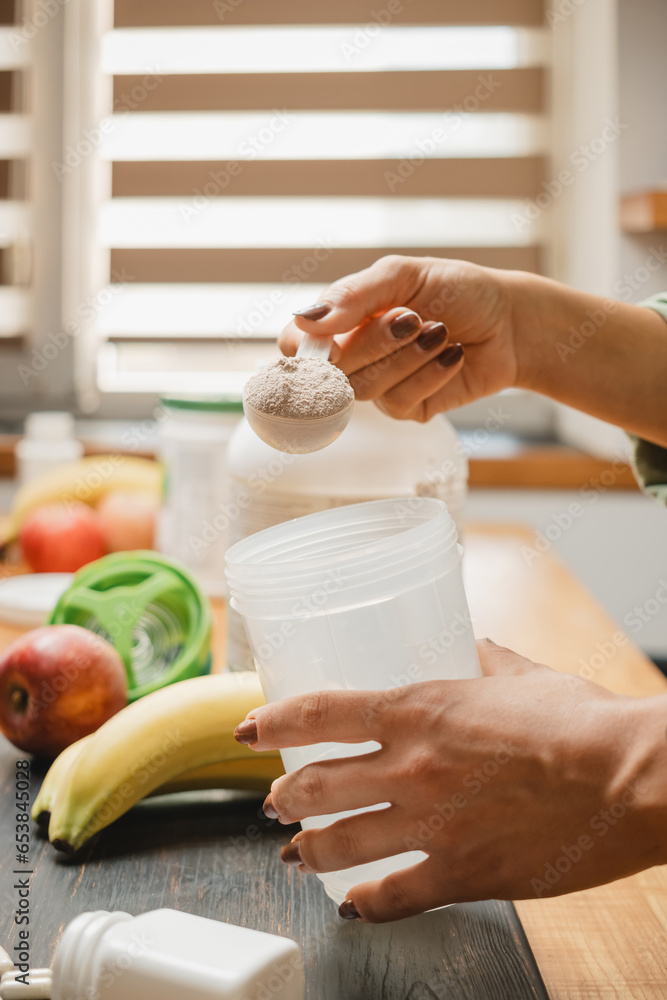 Woman with a measuring spoon in her hand puts portion of whey protein ...