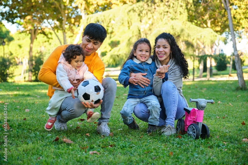 Latin family with two children soccer ball and balance bike in a park ...