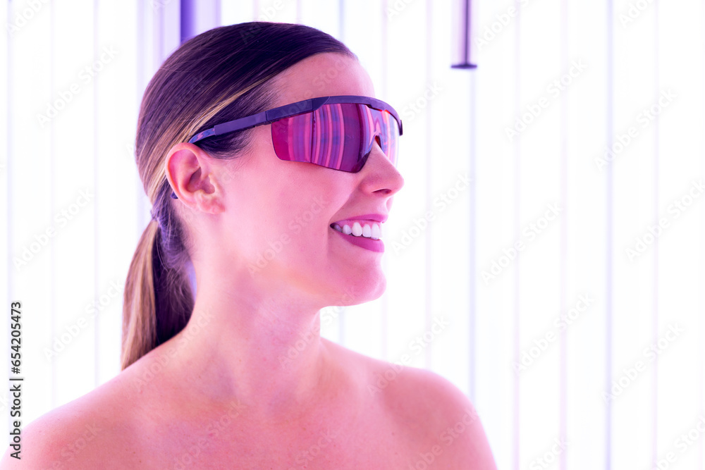 A cute girl is inside a solarium tanning happily with sunglasses ...