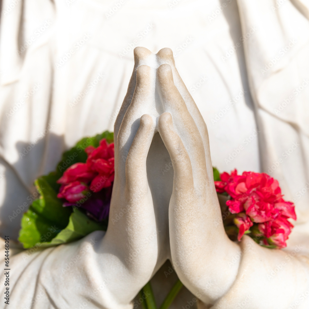 Close up of the praying hands with flowers in them of the statue of the ...