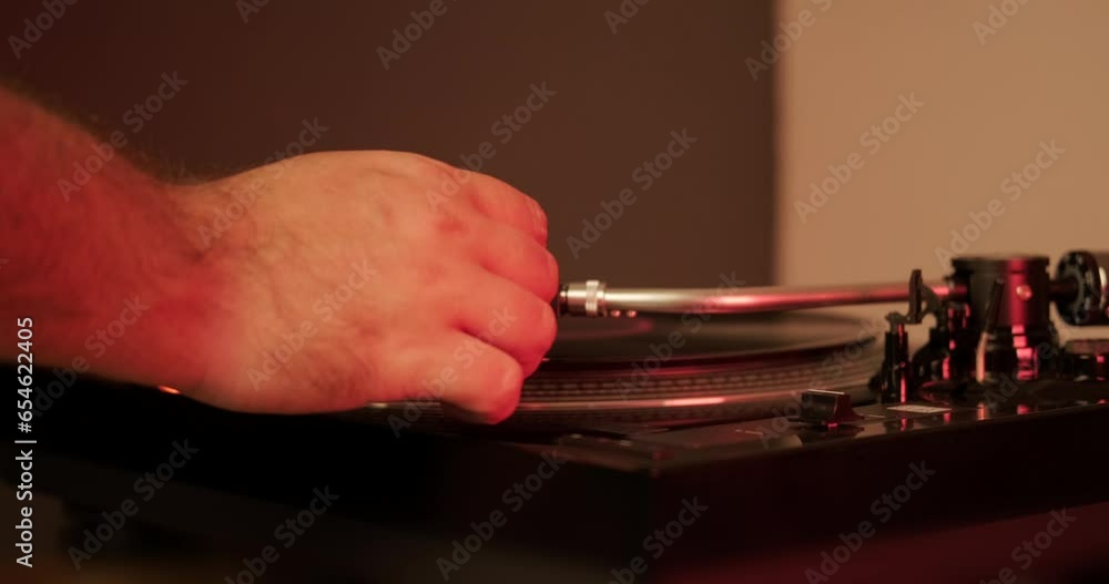 A close-up of a man's hand taking the tonearm and placing it on the ...
