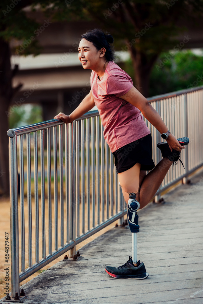 Athlete with prosthetic leg doing warm up exercise on park. Woman ...