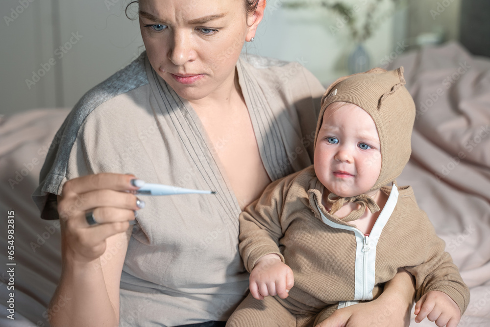 Mom measures body temperature baby by electronic thermometer. Sick child with high temperature ...