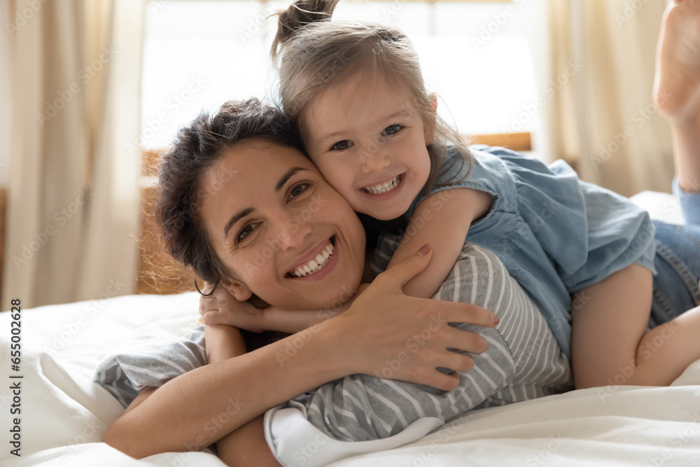 Portrait of cute little girl child lying in bed with happy young mother ...