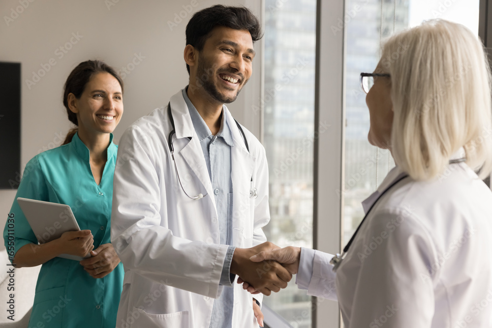 Clinic mature head doctor congratulating younger Indian intern on ...