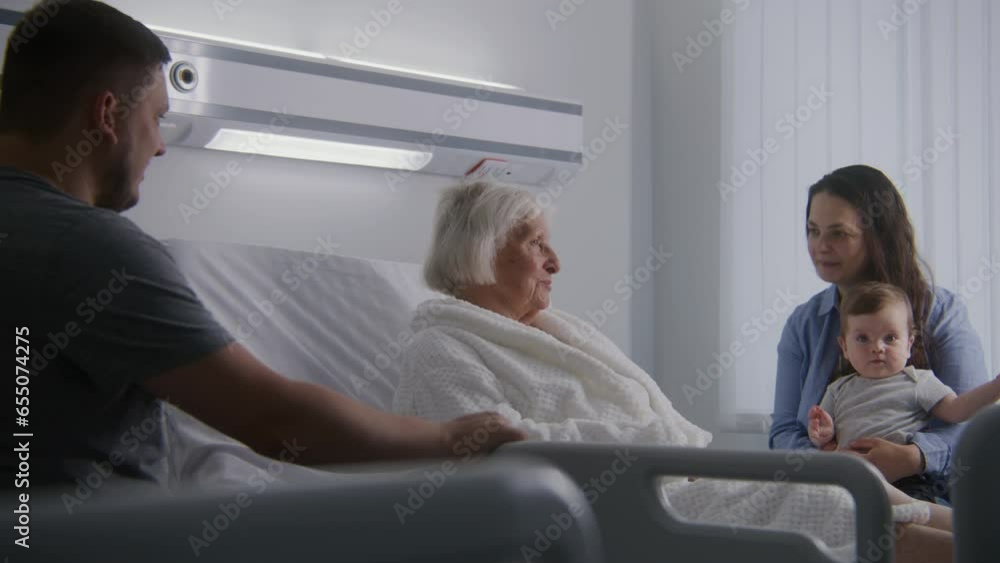 Female old patient lies in bed in bright hospital ward, spends time ...