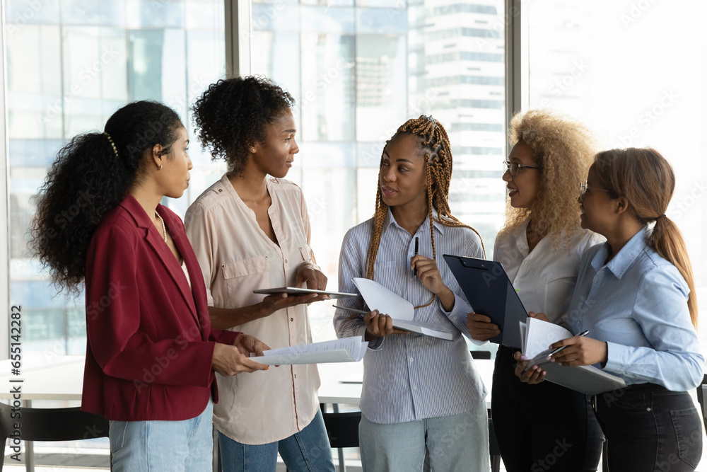 African American businesswomen brainstorming, holding papers, standing ...