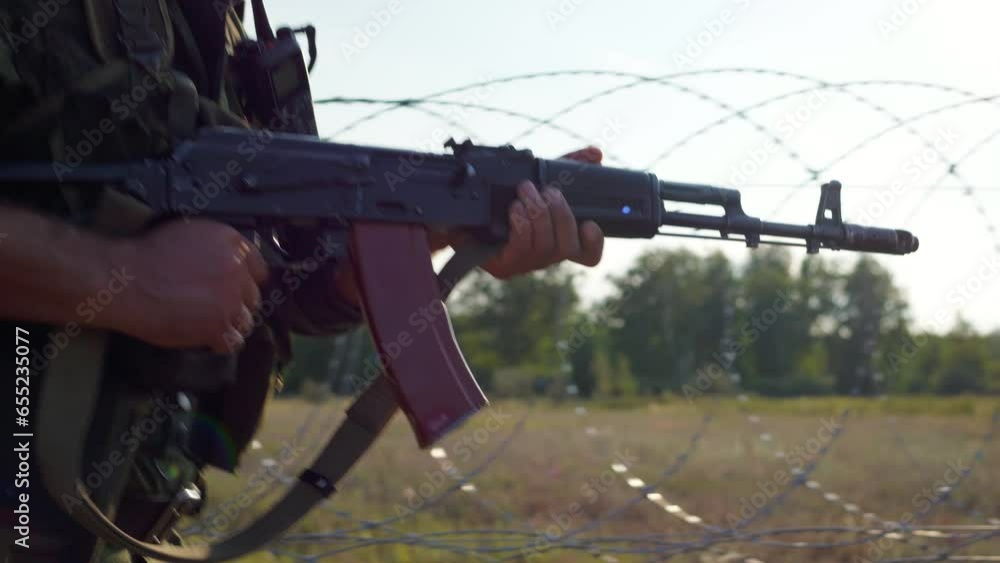 Armed soldier walks along barbed wire wall and patrols border line ...