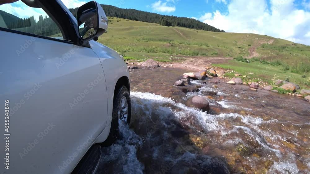 A white SUV drives through the river and mud. View of the wheels. The ...